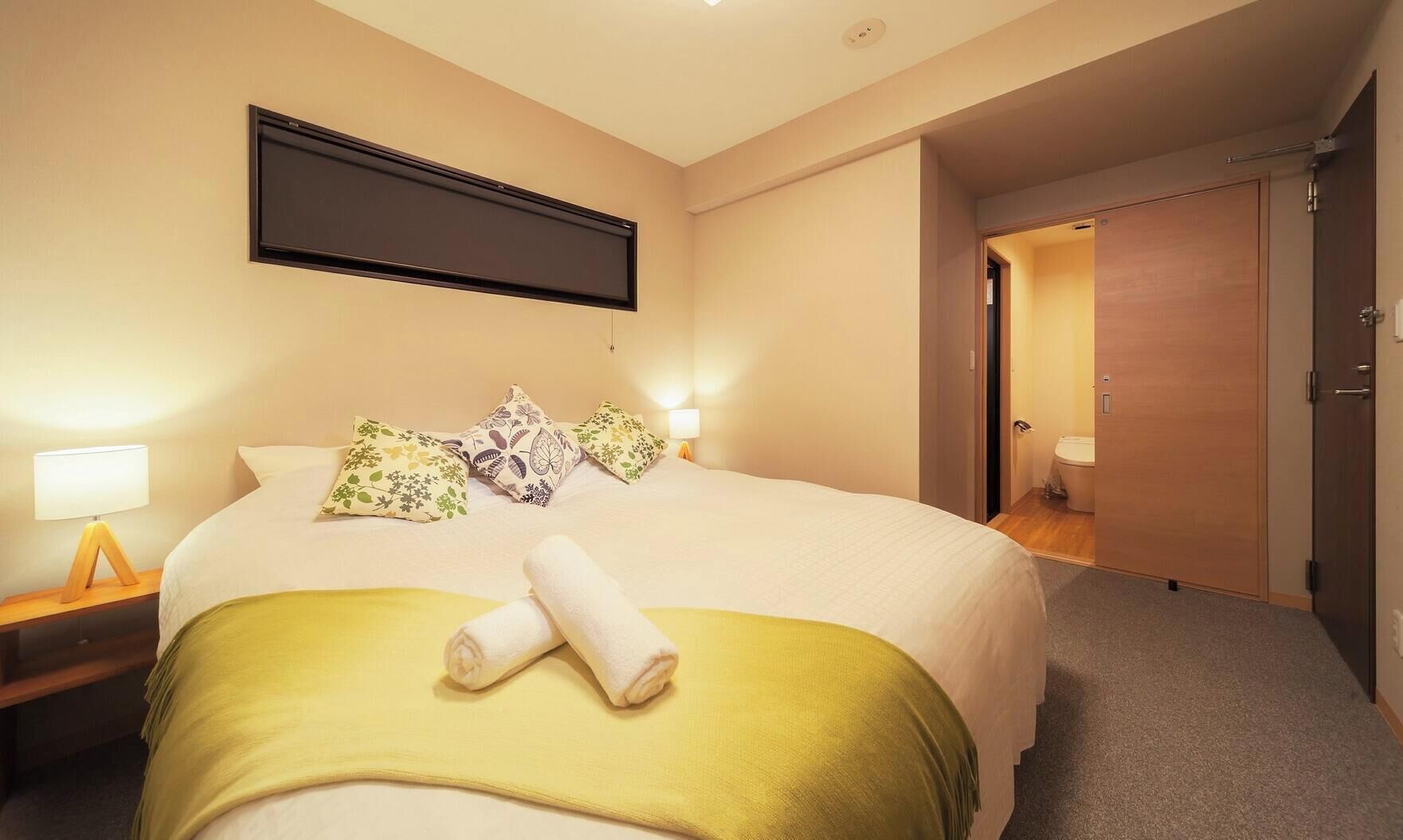 Quarto de hotel com uma cama, televisão fixada na parede, abajur e porta para um banheiro.