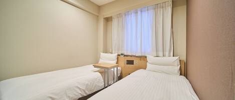 Quarto de hotel com duas camas de solteiro, uma mesinha e uma janela com cortinas.