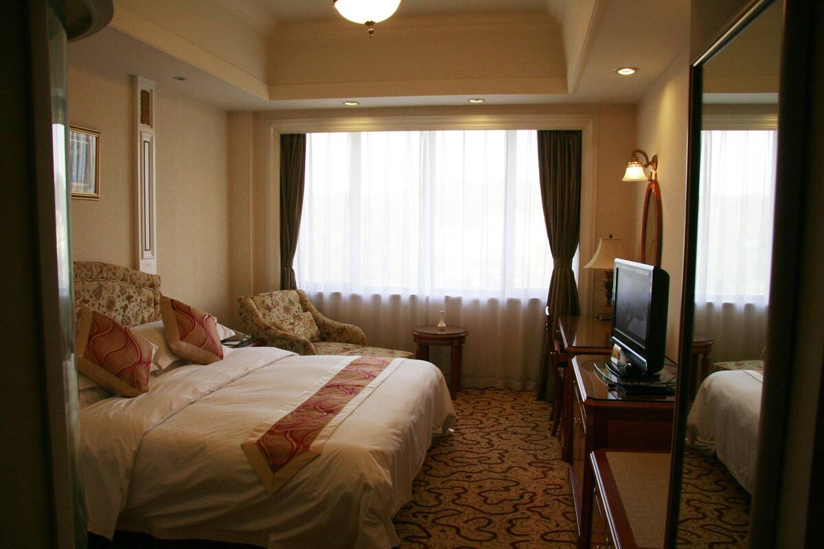 Quarto de hotel com uma cama grande, uma mesa com televisão, uma cadeira e um espelho.