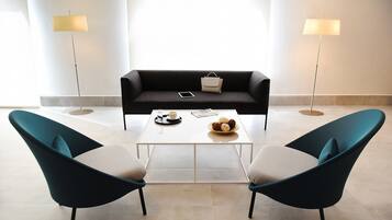Uma sala de estar moderna com um sofá preto, duas poltronas verde-água, uma mesa de centro e duas luminárias de chão.