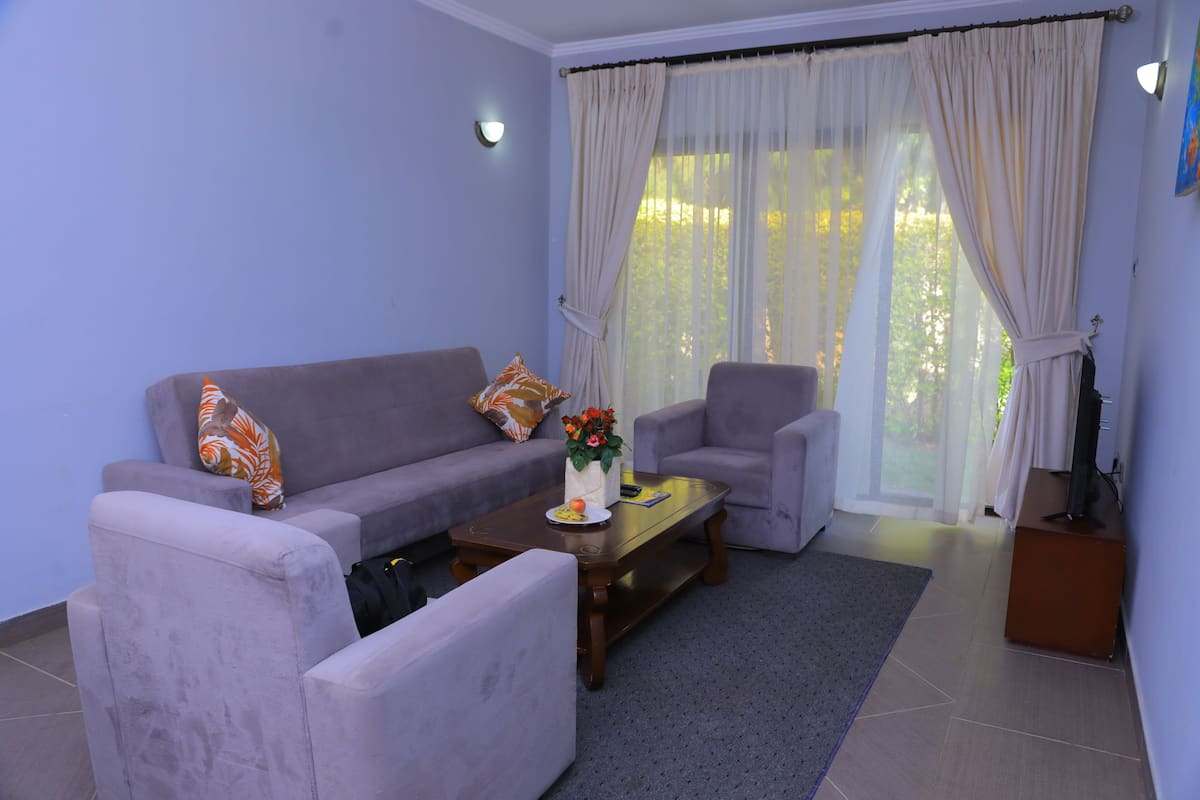 Sala de estar com sofá, poltrona, mesa de centro e cortinas.