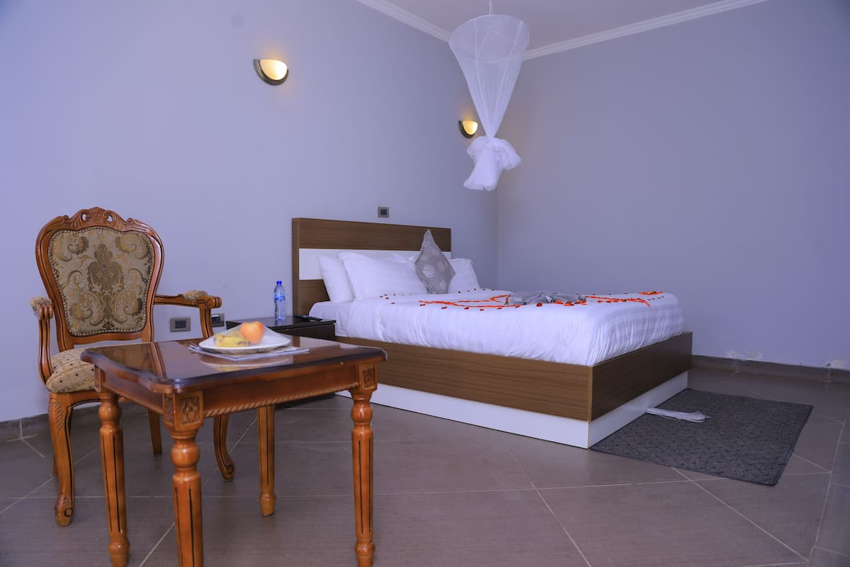 Quarto com cama de madeira, uma cadeira, uma mesa e uma mesa de cabeceira com uma garrafa e um prato.