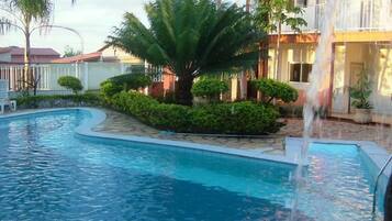 Piscina com cascata, cercada por vegetação bem cuidada e um edifício com varandas.