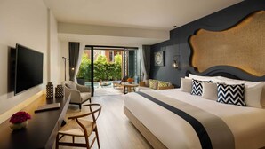 Quarto de hotel moderno com uma cama grande, uma mesa de trabalho e uma TV. Há uma varanda com vista para áreas verdes e uma piscina.