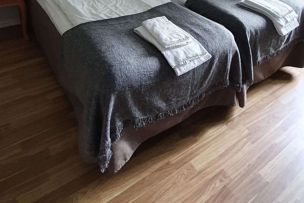 Quarto com duas camas, piso de madeira, ventilador de teto, janela e mesa de cabeceira com abajur.