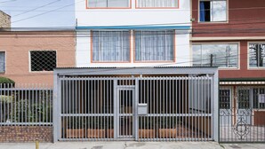 Edifício residencial com entrada protegida por grades, várias janelas e uma caixa de utilidades visível.