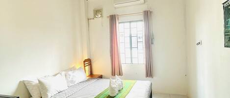Quarto com cama, mesa, ar condicionado e janela com cortinas.