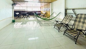 Um quarto com piso de azulejos, uma rede verde e várias cadeiras xadrez.