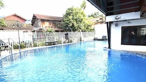 Uma piscina com borda azulejada, cercada por uma cerca branca e casas ao fundo.
