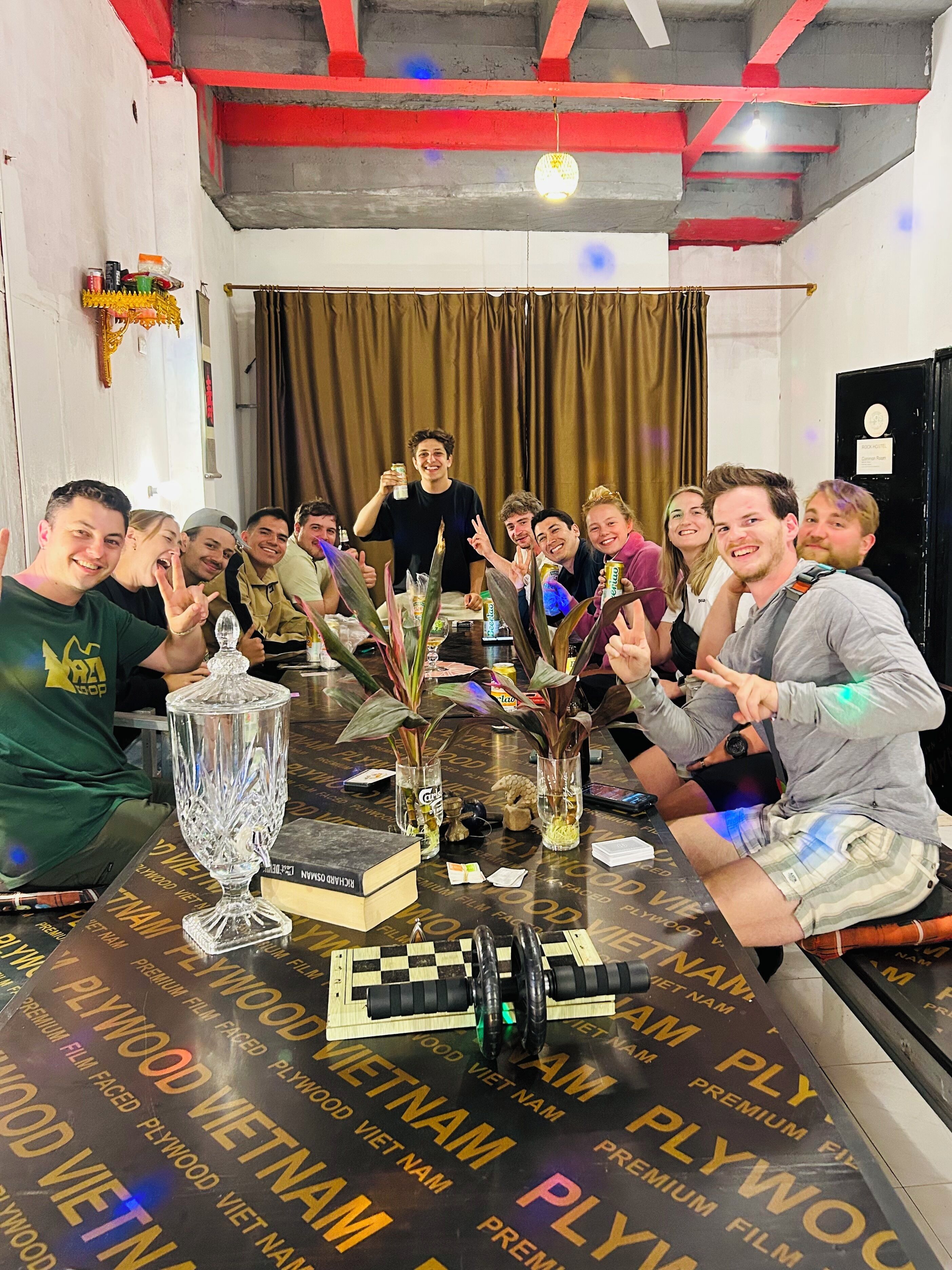 Um grupo de pessoas sentadas à volta de uma mesa, com um troféu grande e livros, num espaço com teto vermelho e cortina.