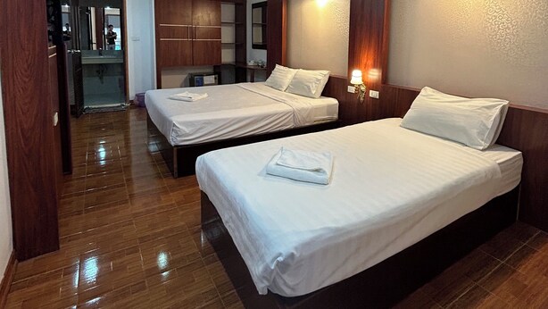 Quarto de hotel com duas camas, piso de madeira, um guarda-roupa e um banheiro visível ao fundo.