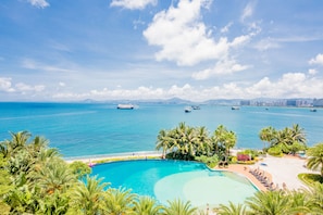 Um resort com uma piscina grande, palmeiras e vista para o mar com barcos.