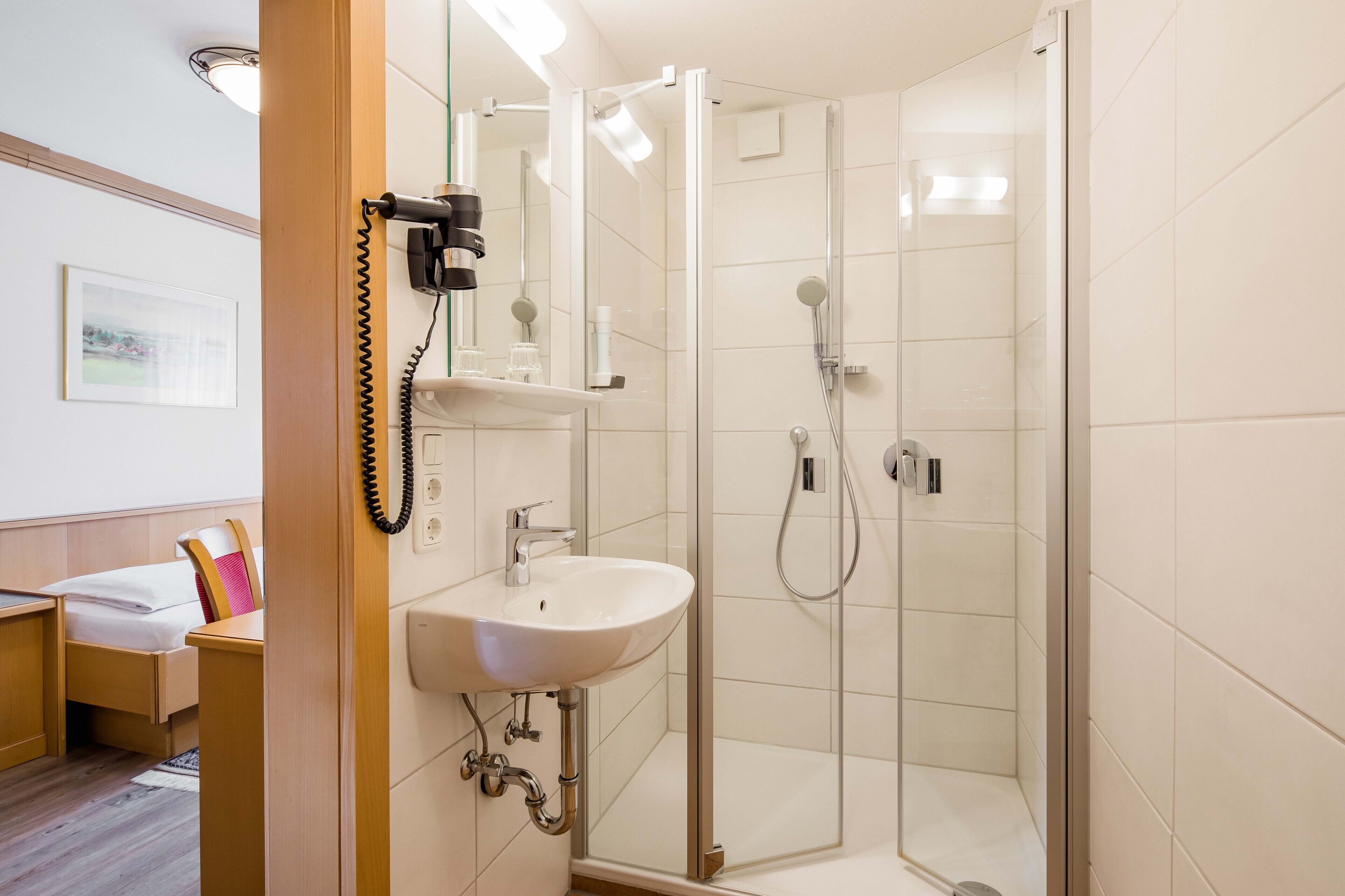 Uma casa de banho moderna com chuveiro de vidro, lavatório e secador de cabelo fixado na parede.