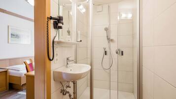 Uma casa de banho moderna com chuveiro de vidro, lavatório e secador de cabelo fixado na parede.