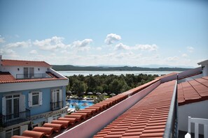 Hotel com telhados em terracota, área de piscina e vista para um lago e montanhas.
