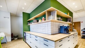Uma cozinha moderna com bancada de madeira, armários brancos e uma parede verde de destaque. Há prateleiras com copos e eletrodomésticos.