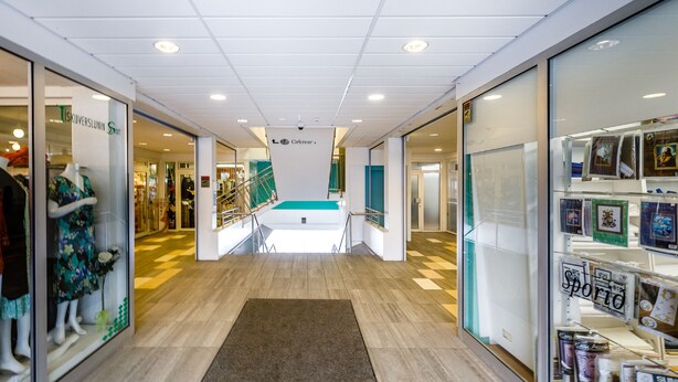 Um corredor com escadaria central, vitrines de vidro em ambos os lados e piso padronizado.