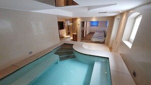 Uma piscina interior moderna com design curvo, uma escadaria que leva a um quarto e uma grande janela que proporciona luz natural.