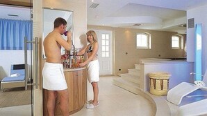 Casa de banho moderna com cabine de duche em vidro, toucador com espelho e um pequeno espaço de estar com uma cadeira e um cesto.