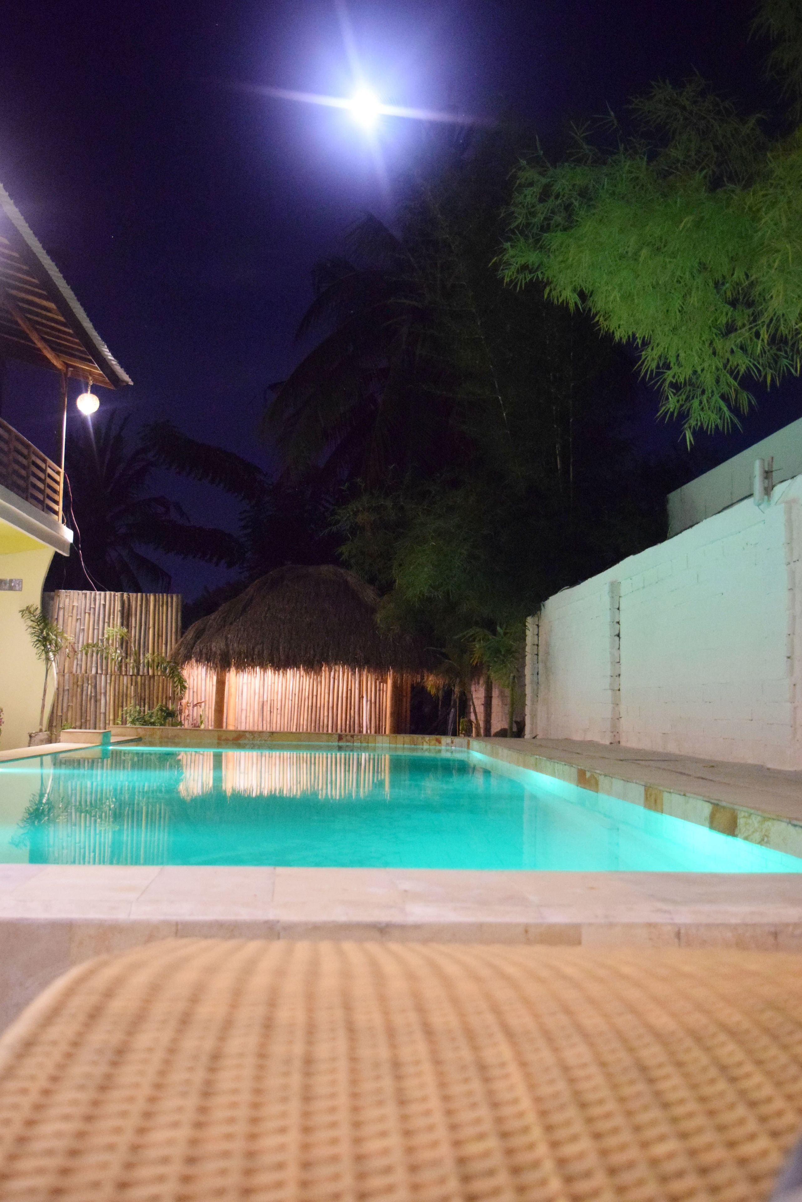 Piscina à noite com uma estrutura coberta de palha ao fundo.