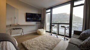 Uma sala de estar moderna com uma janela grande, uma TV de tela plana, um ventilador vertical e uma área de estar aconchegante.