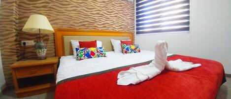 Quarto de hotel com cama, mesa de cabeceira, abajur e janela com persianas.