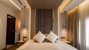 Quarto de hotel moderno com cama grande, mesas de cabeceira, telefone e luminária na parede.