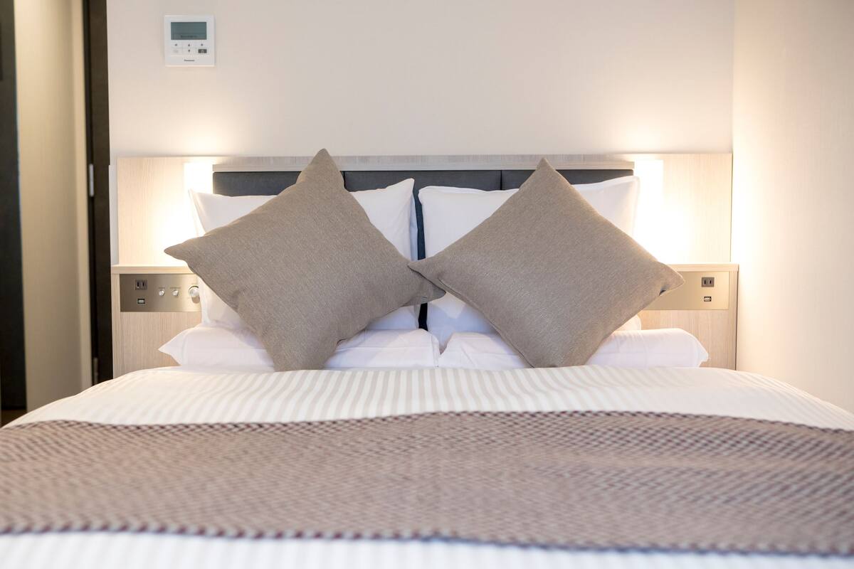 Cama bem arrumada com cabeceira, duas almofadas e um cobertor.
