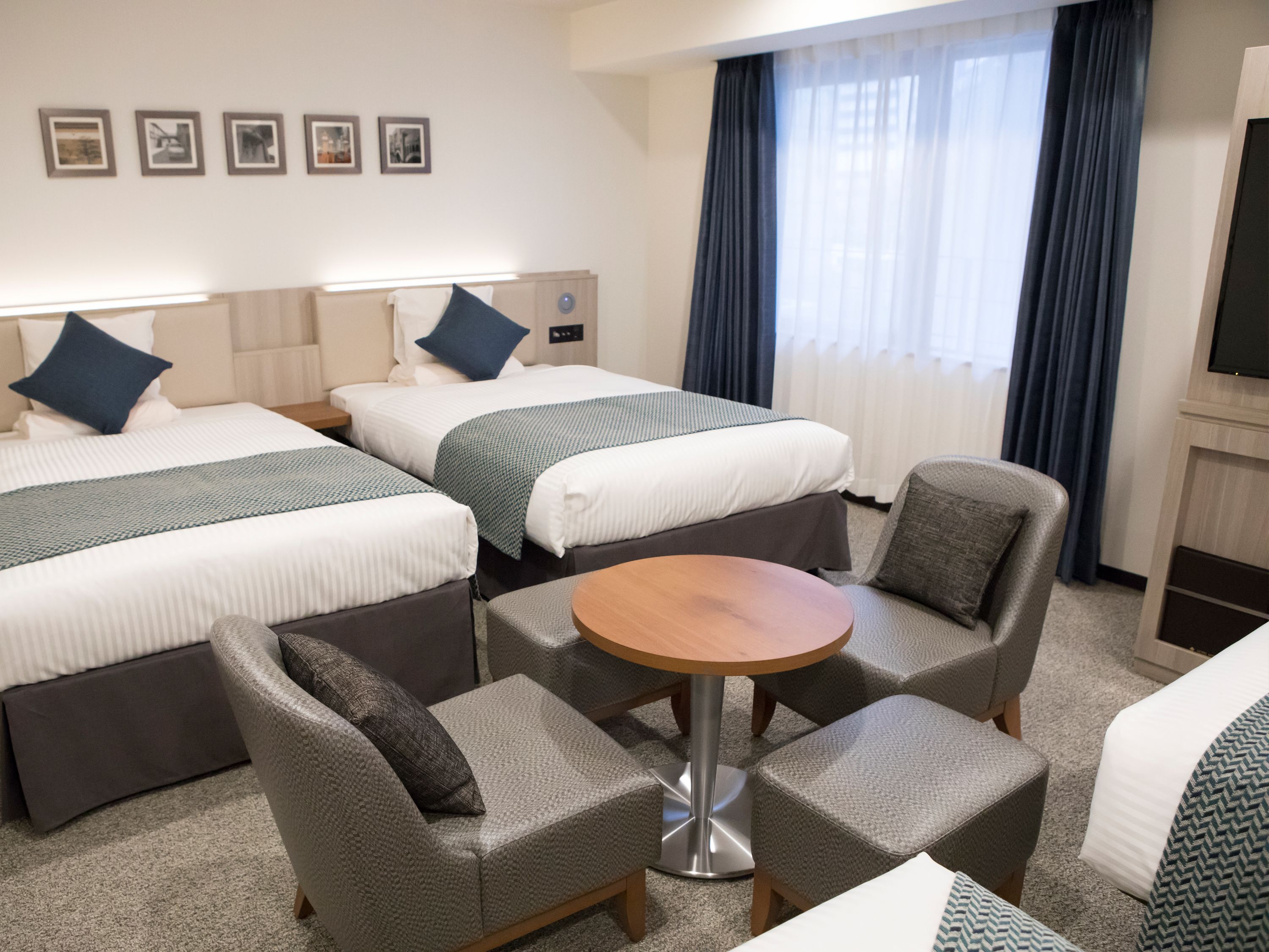 Quarto de hotel com duas camas, uma mesa redonda e duas poltronas.