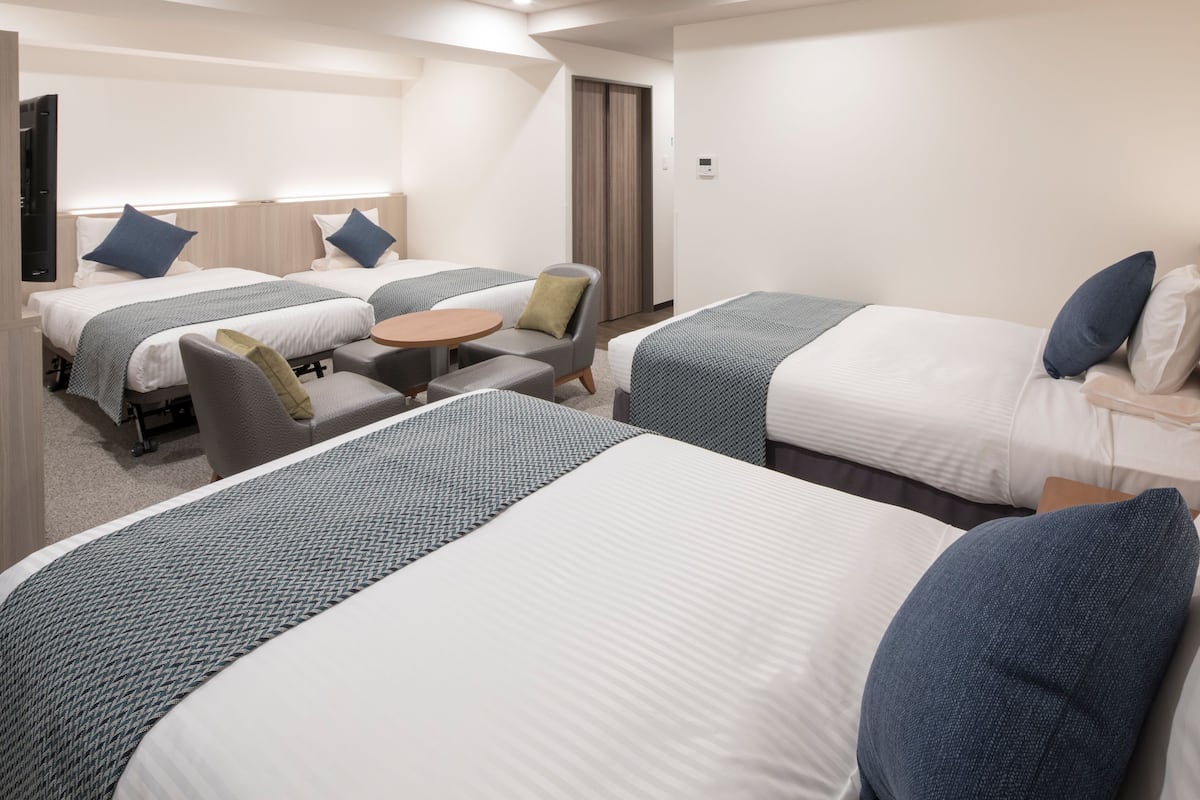 Quarto de hotel com três camas, uma mesa redonda pequena e uma televisão.