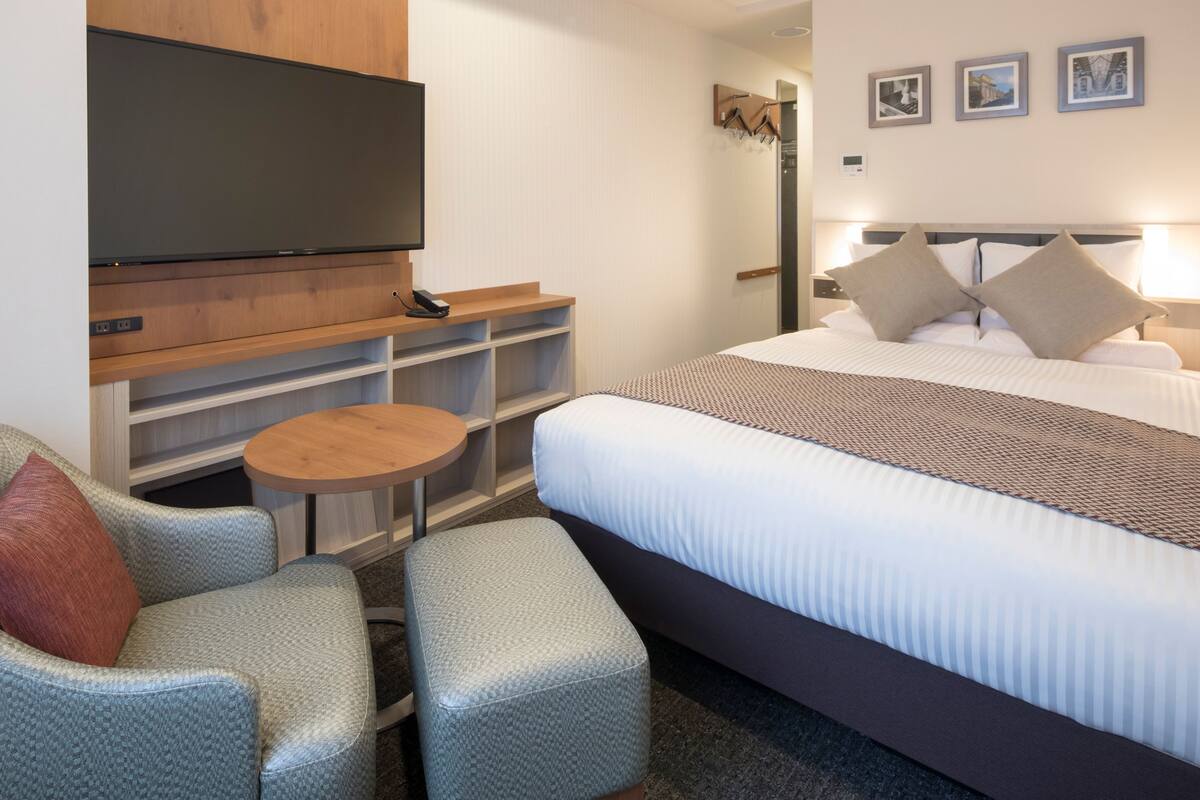 Quarto de hotel com cama, televisão, escrivaninha e cadeira.