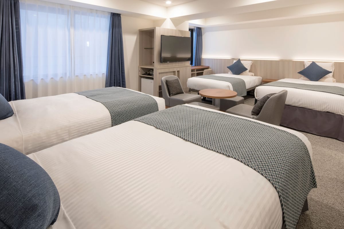 Quarto de hotel com duas camas, televisão, escrivaninha e uma cadeira.
