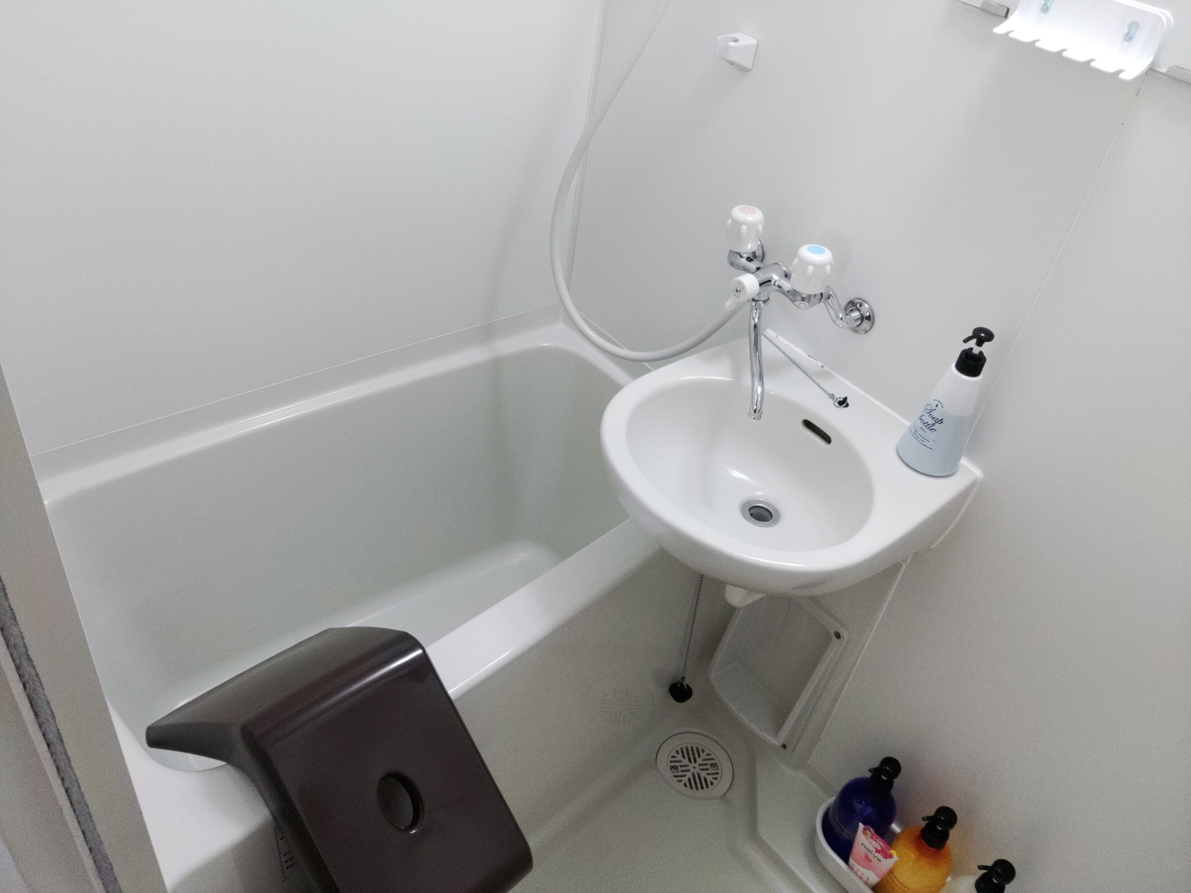 Um banheiro com pia branca, banheira e vaso sanitário. Há artigos de higiene pessoal no chão.