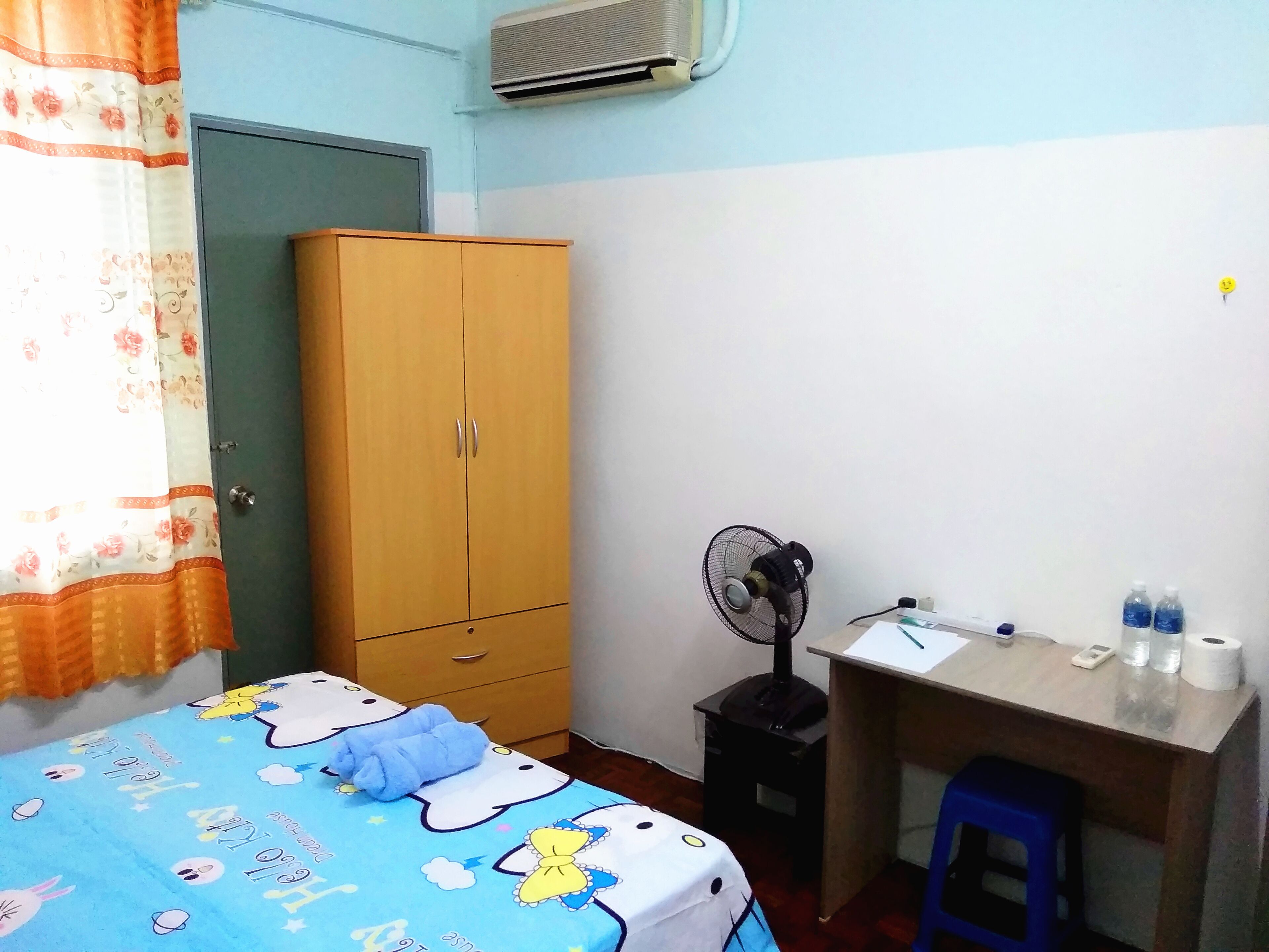 Quarto com cama, guarda-roupa, escrivaninha, ventoinha e banquinho.