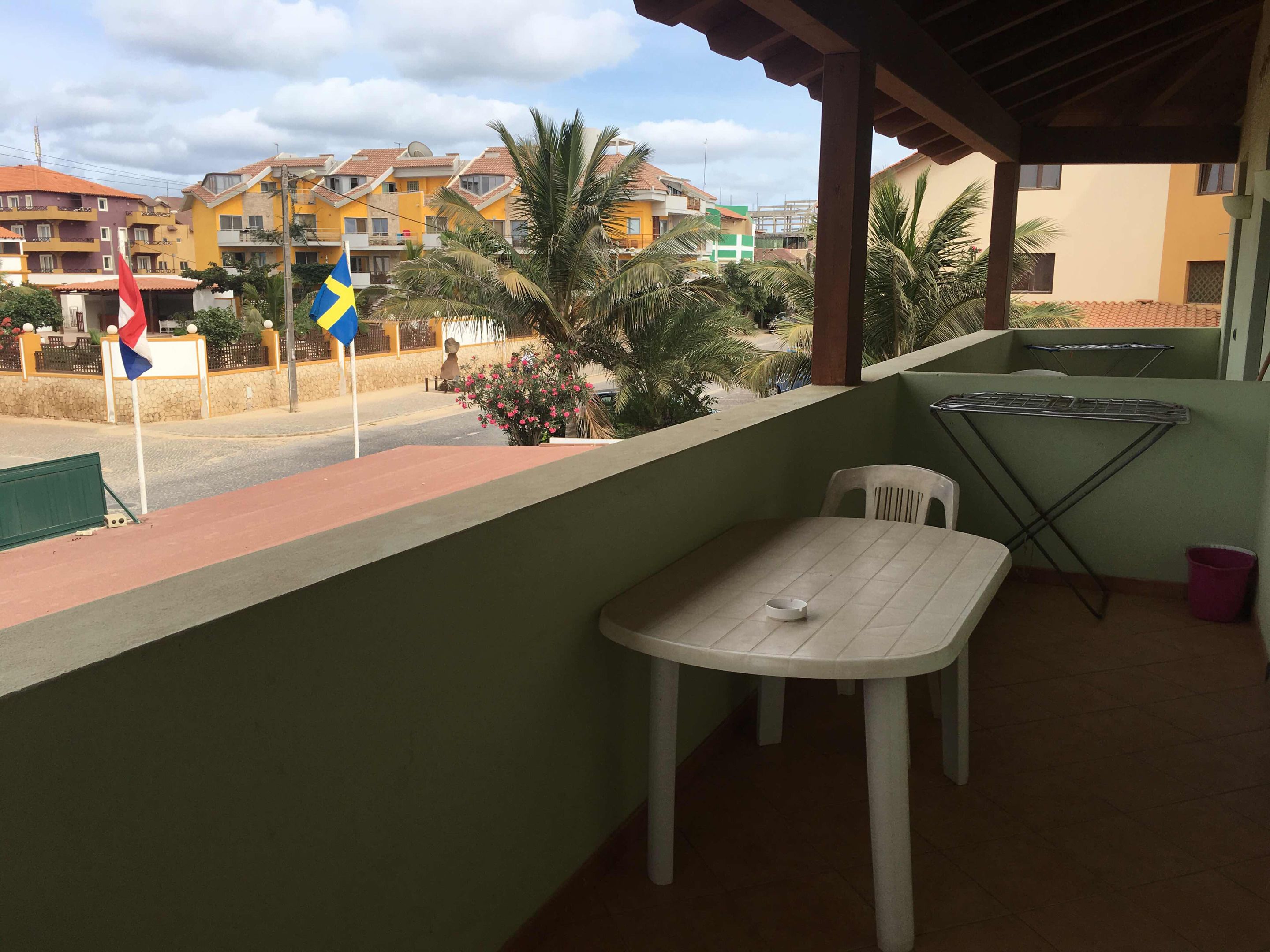 Uma varanda com uma mesa e cadeiras brancas, um varal e uma bandeira.