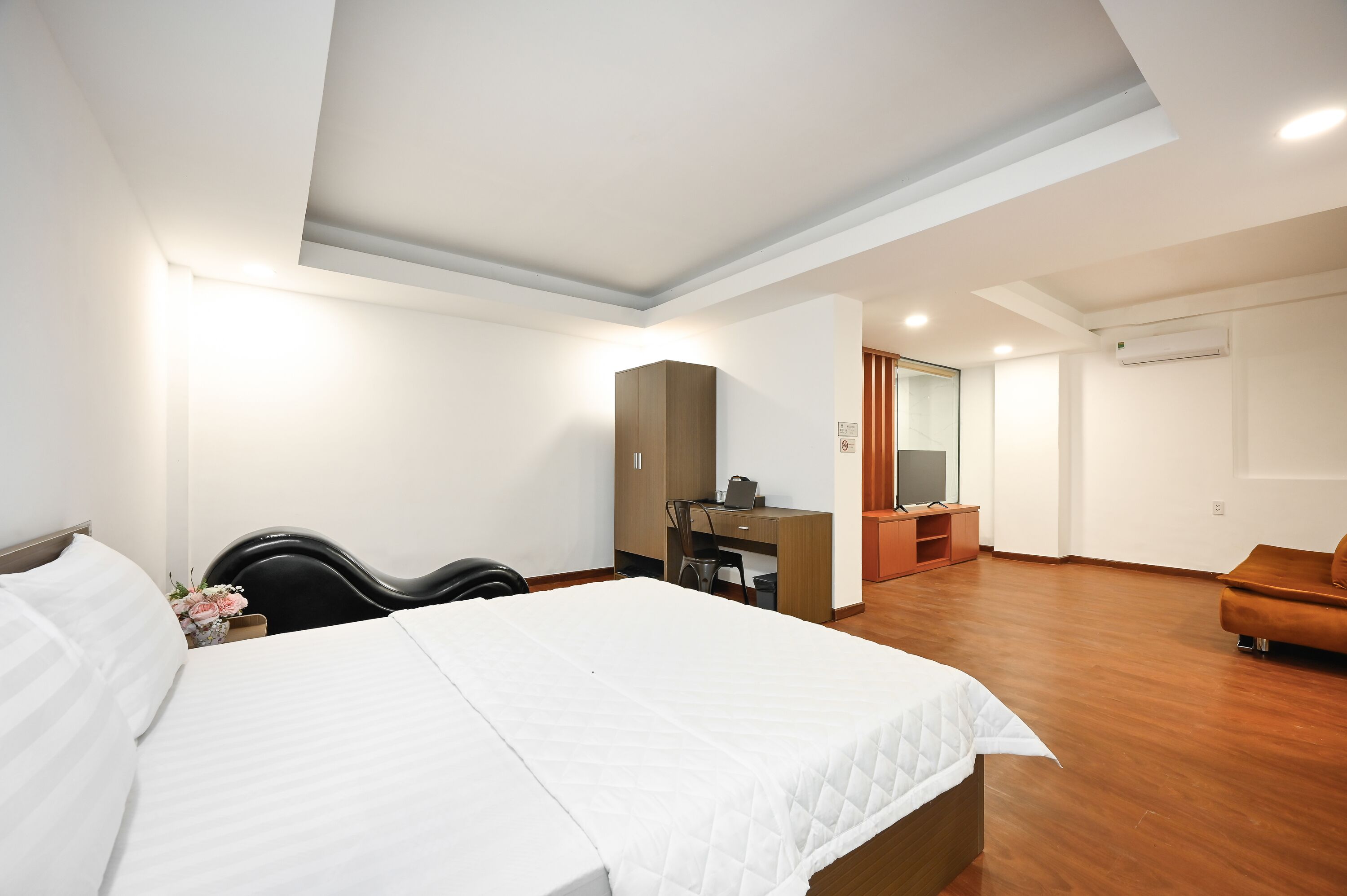Quarto de hotel com uma cama grande, uma escrivaninha, uma cadeira, uma televisão e um sofá.