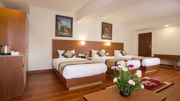 Quarto de hotel com duas camas, piso de madeira, uma escrivaninha com um vaso de flores e luminárias fixadas na parede.