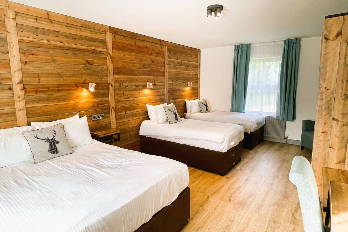 Quarto de hotel com duas camas, painéis de madeira nas paredes e janela com cortinas.