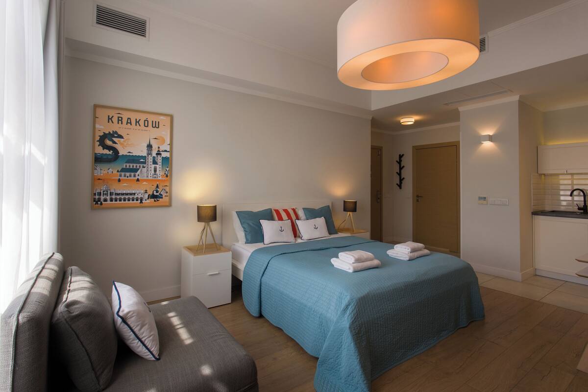 Quarto moderno com cama, mesas de cabeceira, sofá, um pôster e um espaço de cozinha.