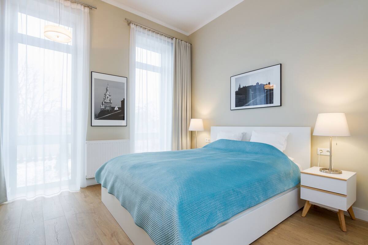 Quarto bem arrumado com cama, duas mesas de cabeceira e duas luminárias de parede.