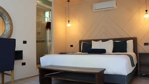 Quarto de hotel com cama, mesas de cabeceira, um banco, unidade de ar condicionado e espelho fixado na parede.