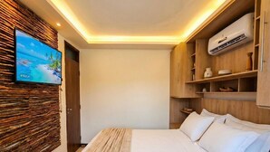 Quarto de hotel com uma cama, televisão na parede, prateleira de madeira e ar condicionado.
