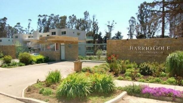 Entrada fechada por portão para um complexo residencial chamado Barrio Golf, com área de jardim ajardinada.