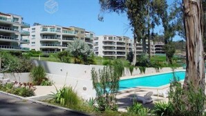 Edifício residencial com várias varandas, piscina e vegetação ao redor.