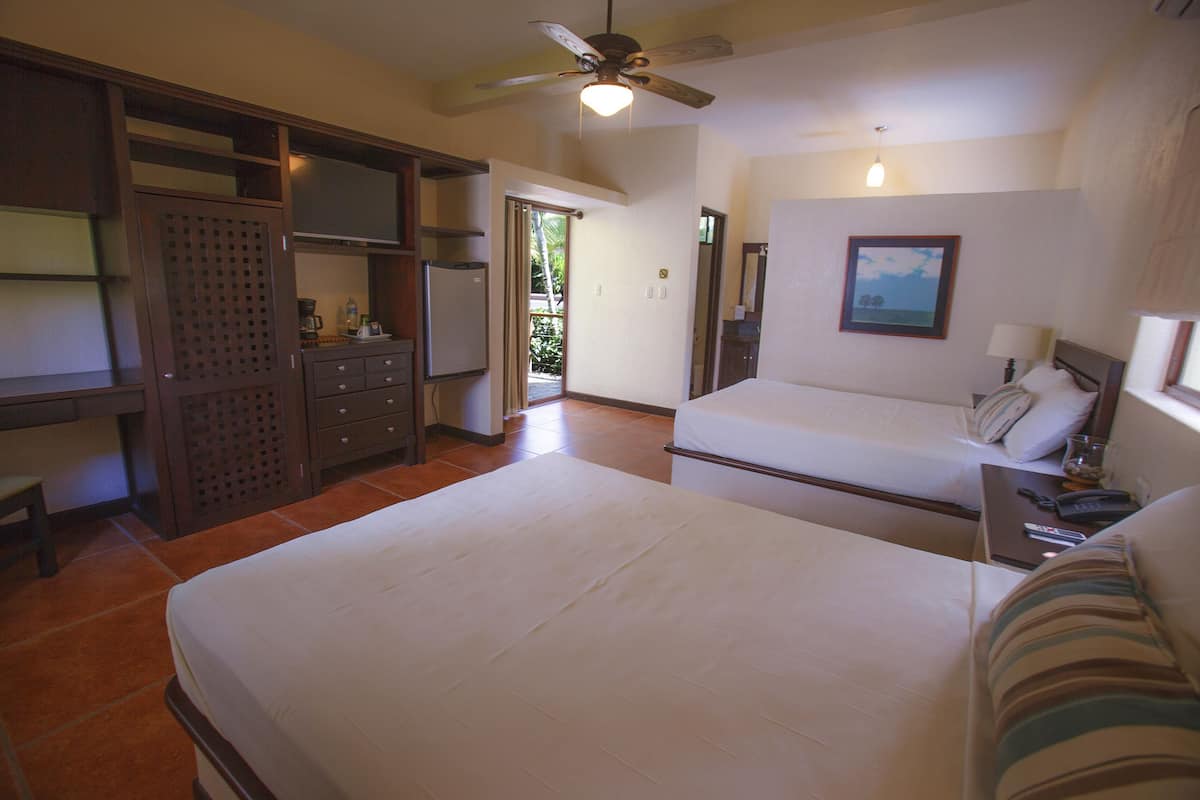 Quarto de hotel com duas camas, uma escrivaninha, um guarda-roupa e um ventilador de teto.
