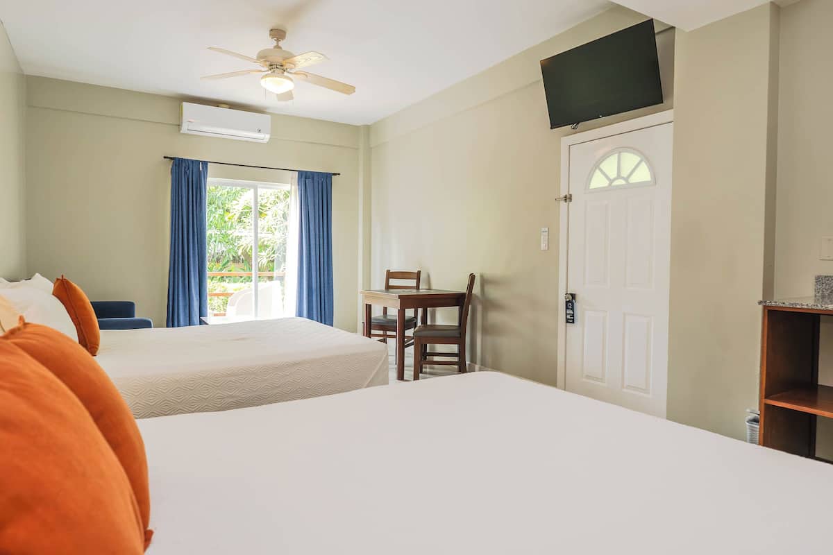 Quarto de hotel com duas camas, uma escrivaninha, uma cadeira, uma televisão e uma porta com janela.