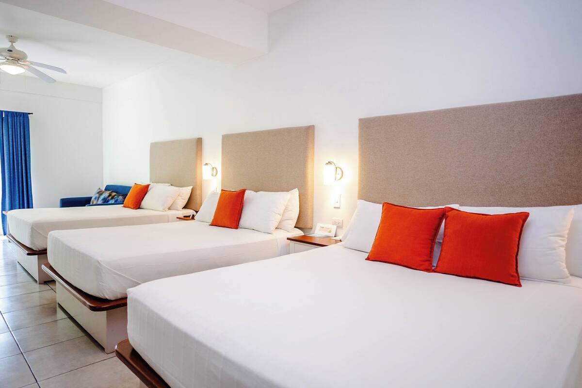 Quarto de hotel com três camas de solteiro, cada uma com cabeceira e mesas de cabeceira.
