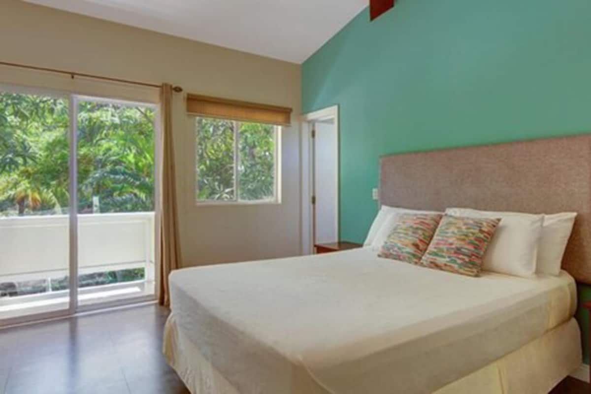 Quarto com uma cama grande, uma parede verde e uma porta de vidro que se abre para uma varanda.