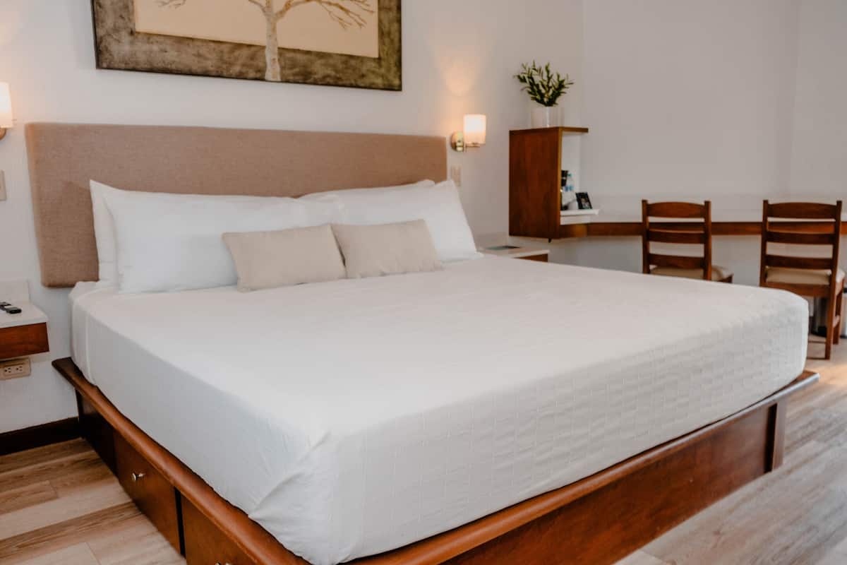 Uma cama bem arrumada com cabeceira de madeira, uma mesa de cabeceira com abajur e uma cadeira em um quarto com design simples e clean.