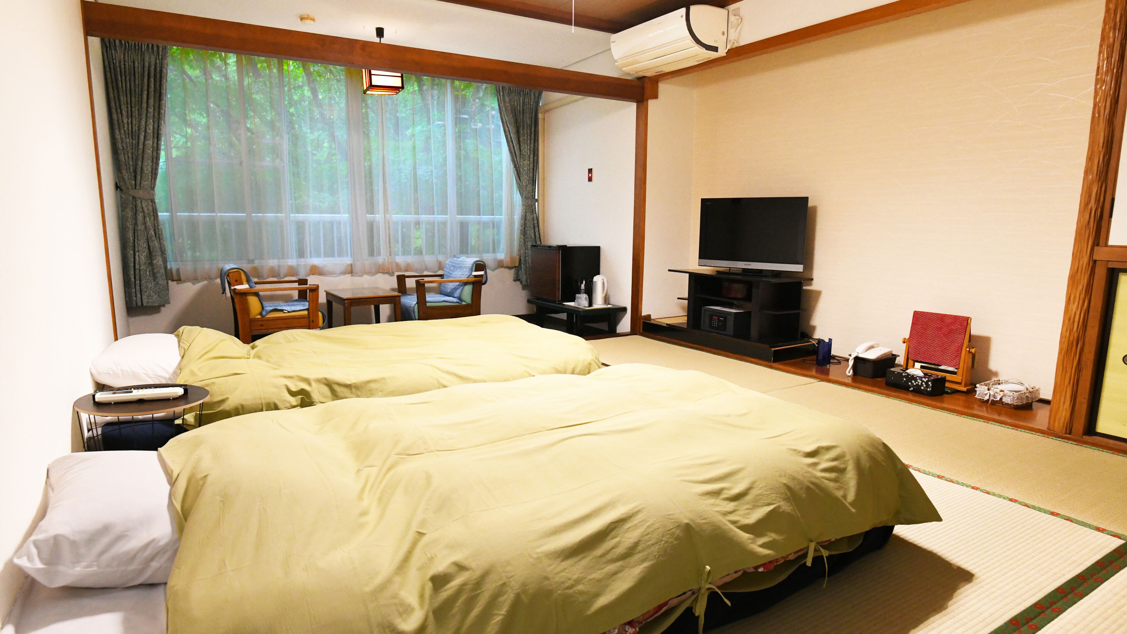 Quarto de hotel com duas camas, televisão, escrivaninha e vista para o exterior.